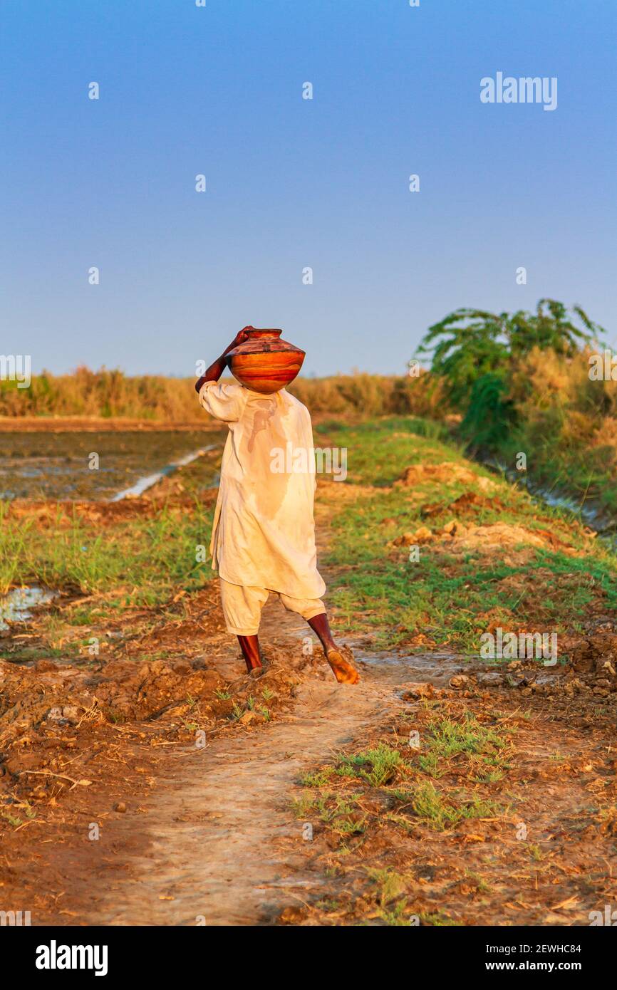 A farmer carrying a large clay dish on his shoulder walking across a ...