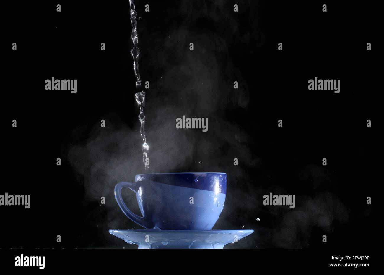Pouring very hot water into a cup against a black background and ...