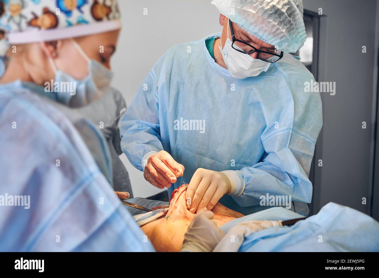 Medical team in sterile gloves performing plastic surgery in operating ...