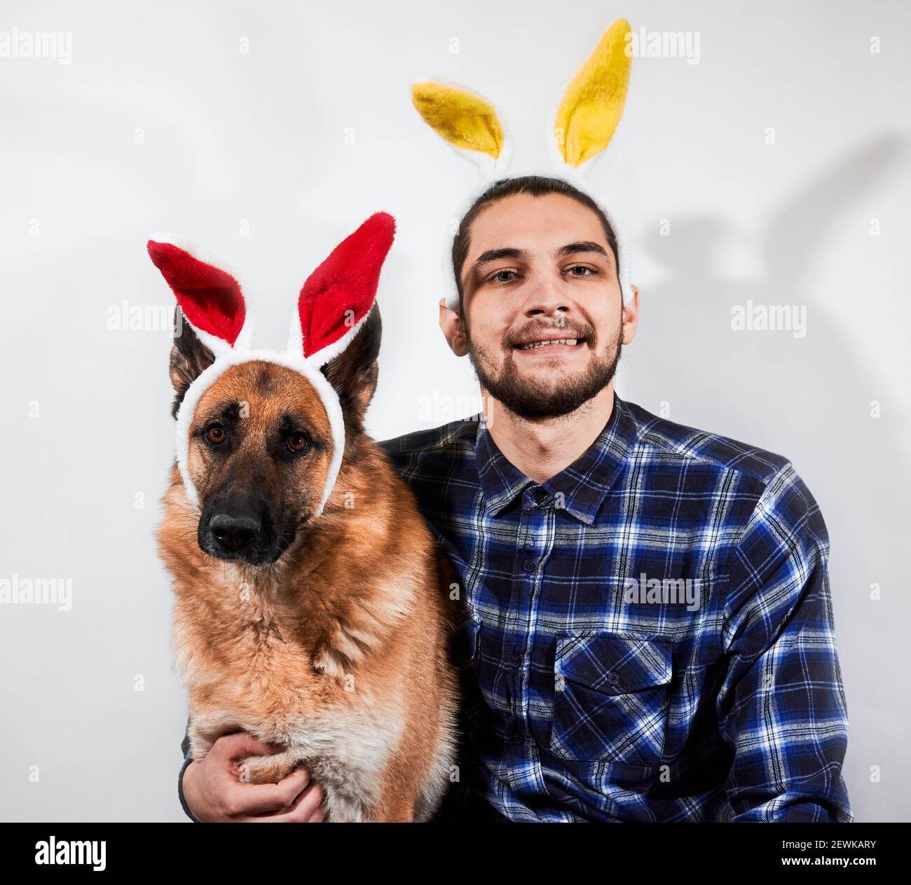 Caucasian man with beard and yellow rabbit ears hugs German shepherd ...