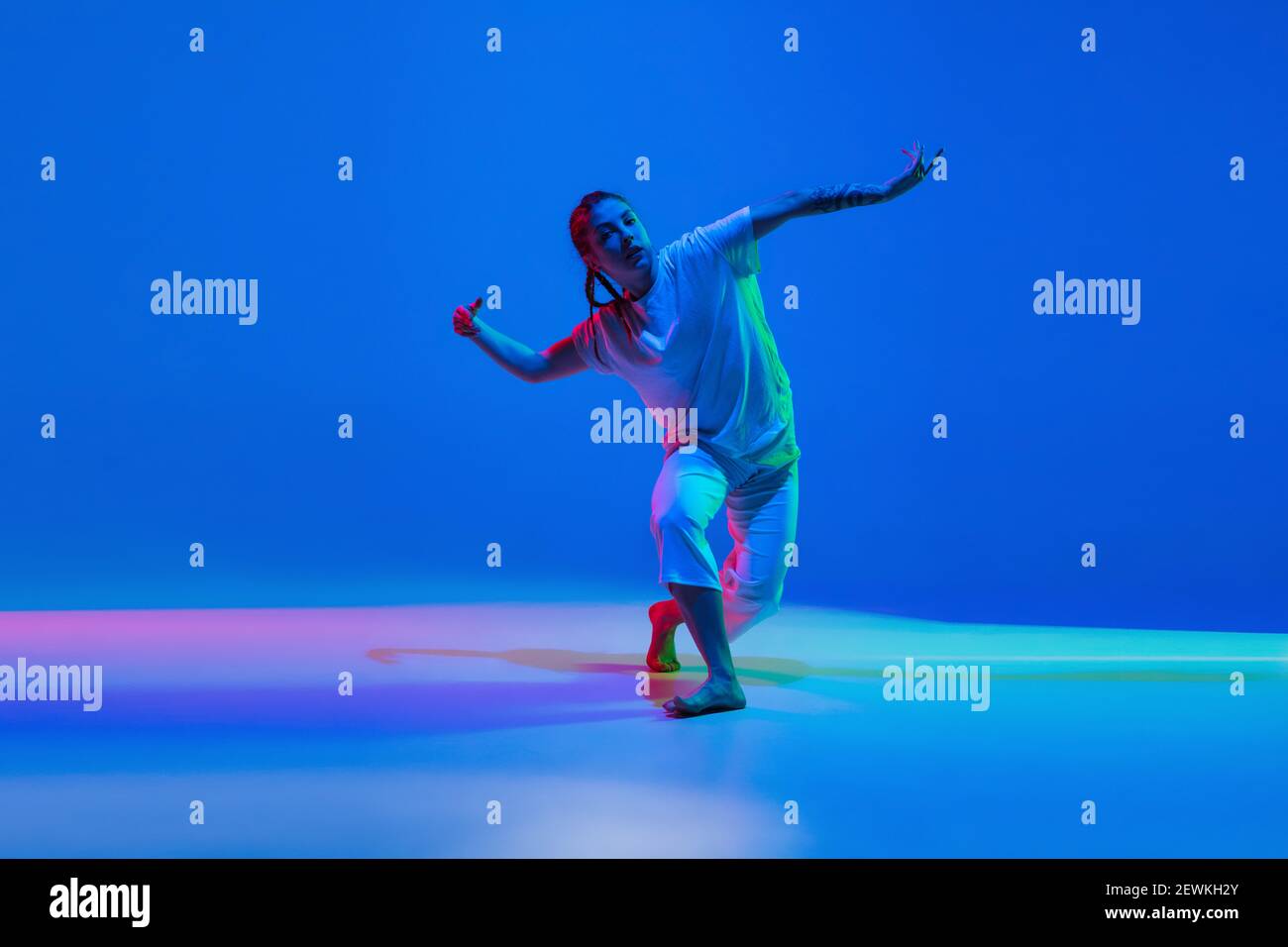 Beautiful girl dancing hip-hop in white attire on blue background in ...
