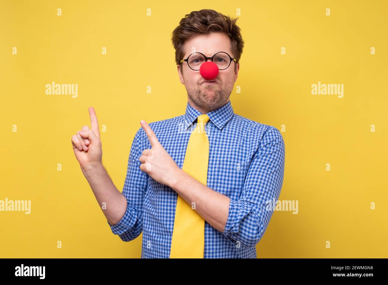 Angry caucasian man with red clown nose pointing aside with hand ...