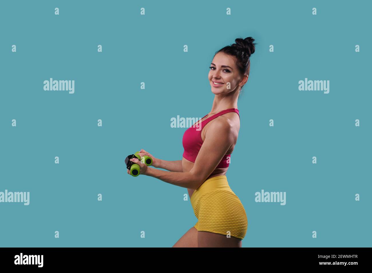 Side view of a beautiful slender woman holding dumbbells and pumping ...