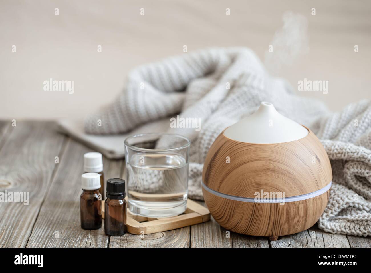 Modern aroma oil diffuser on wood surface with knitted element, water and oils in jars Stock ...