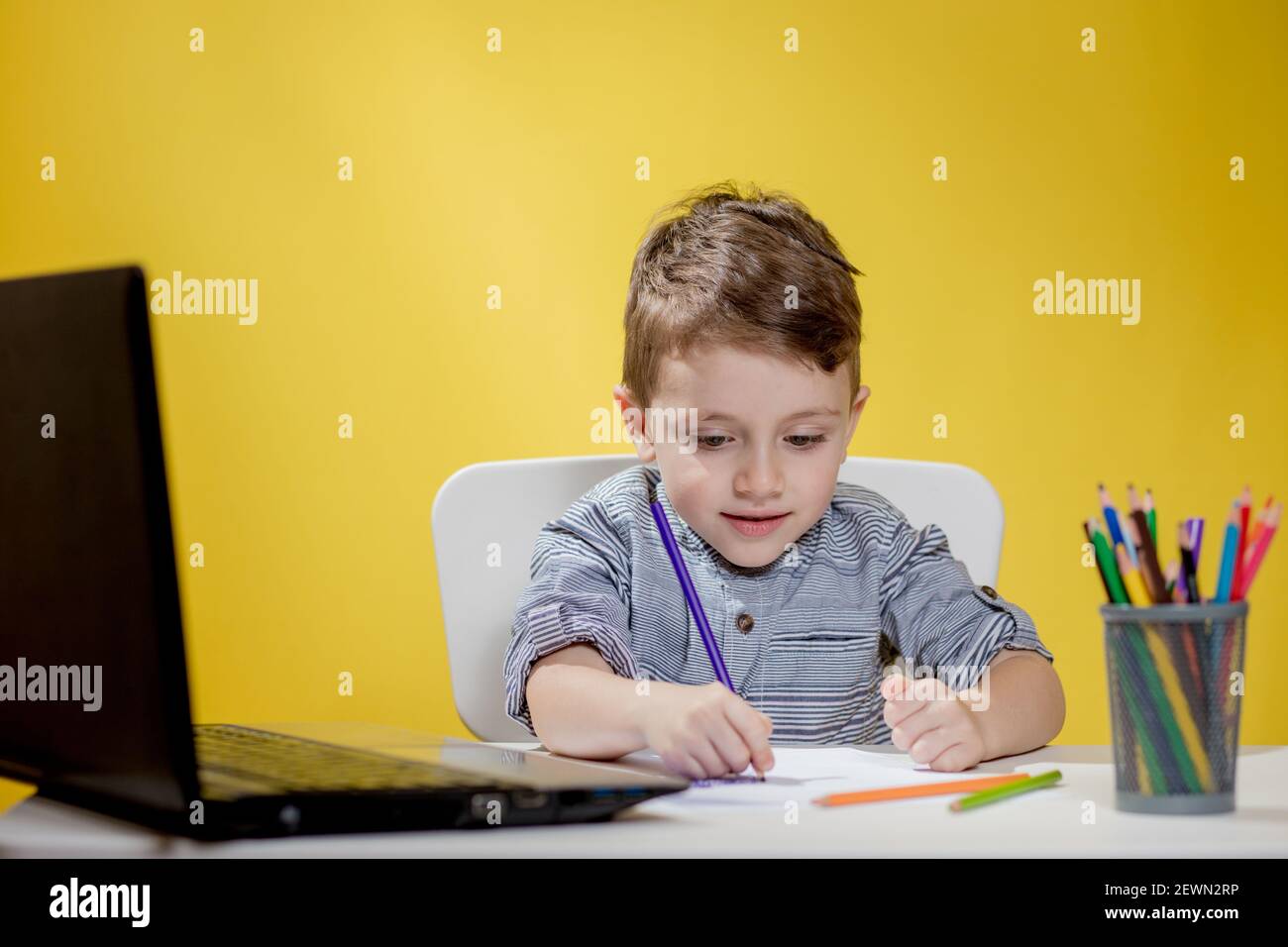 Happy Child using digital laptop doing homework on yellow background ...