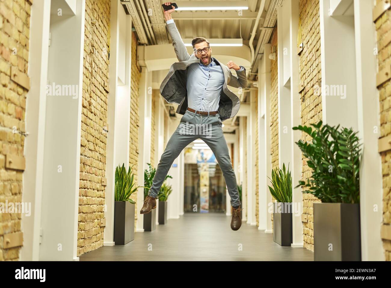 Positive young man in a suit jumping high in excitement and putting ...