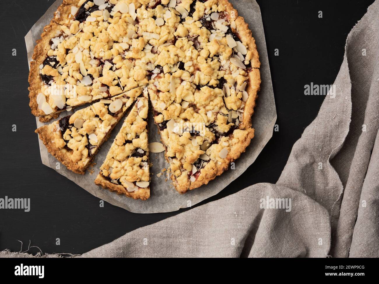 baked round crumble pie with plum cut into pieces on a black background ...