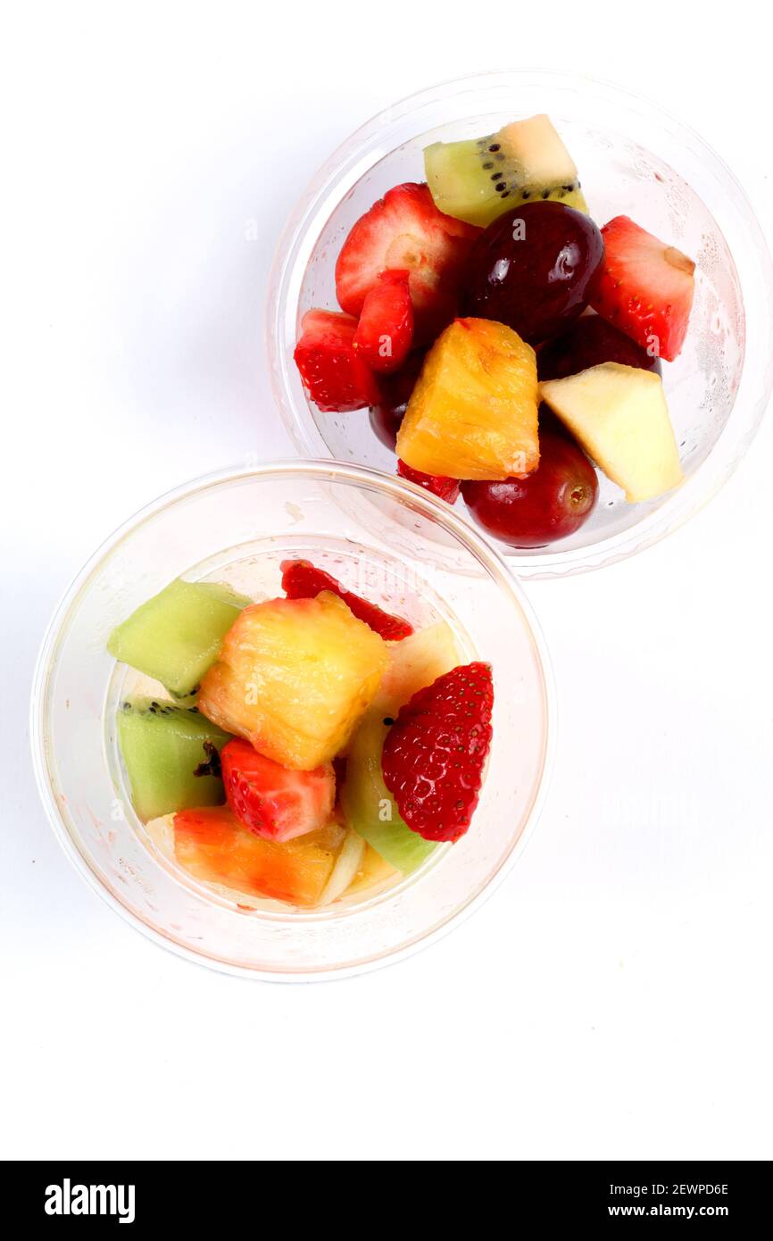 A top view of fresh sliced fruits in plastic cups on white background ...