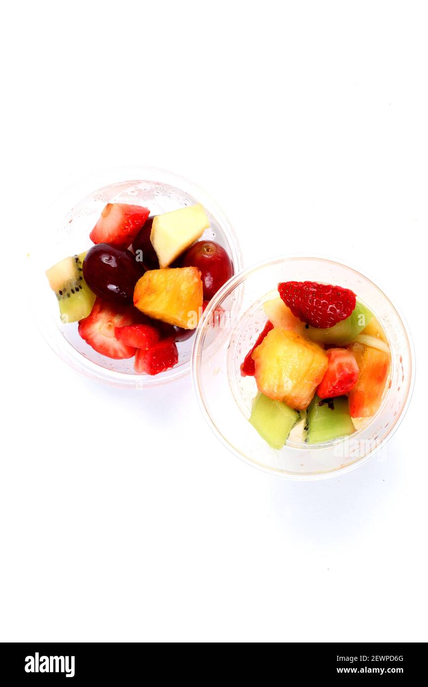 A top view of fresh sliced fruits in plastic cups on white background ...