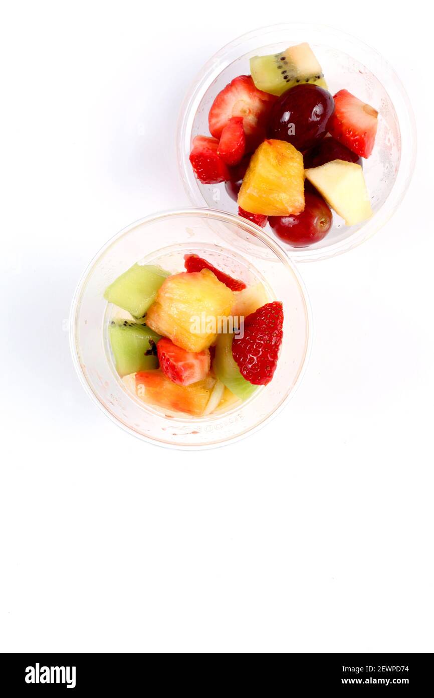 A top view of fresh sliced fruits in plastic cups on white background ...