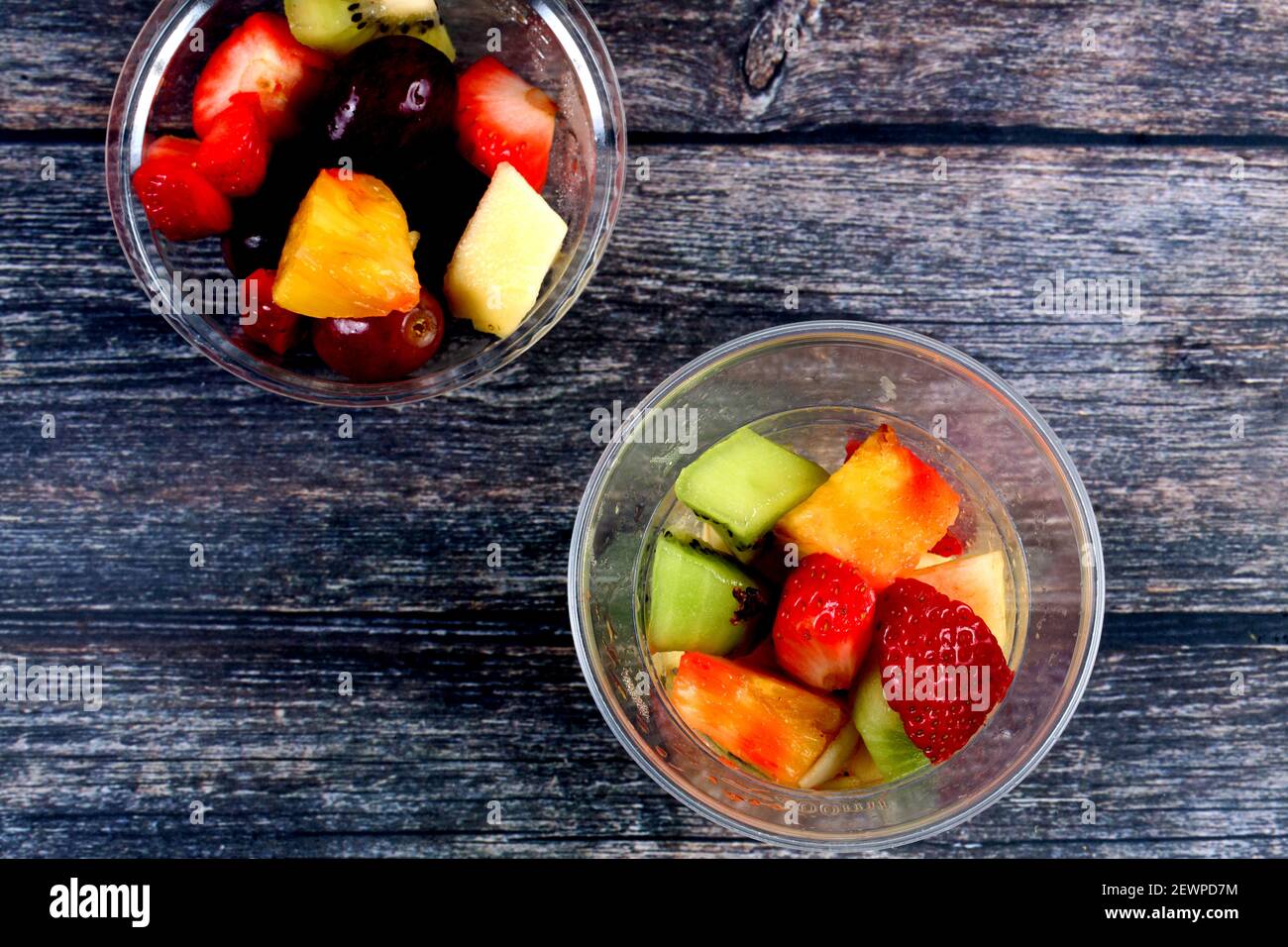 A top view of resh sliced fruits in plastic cups on wooden background ...