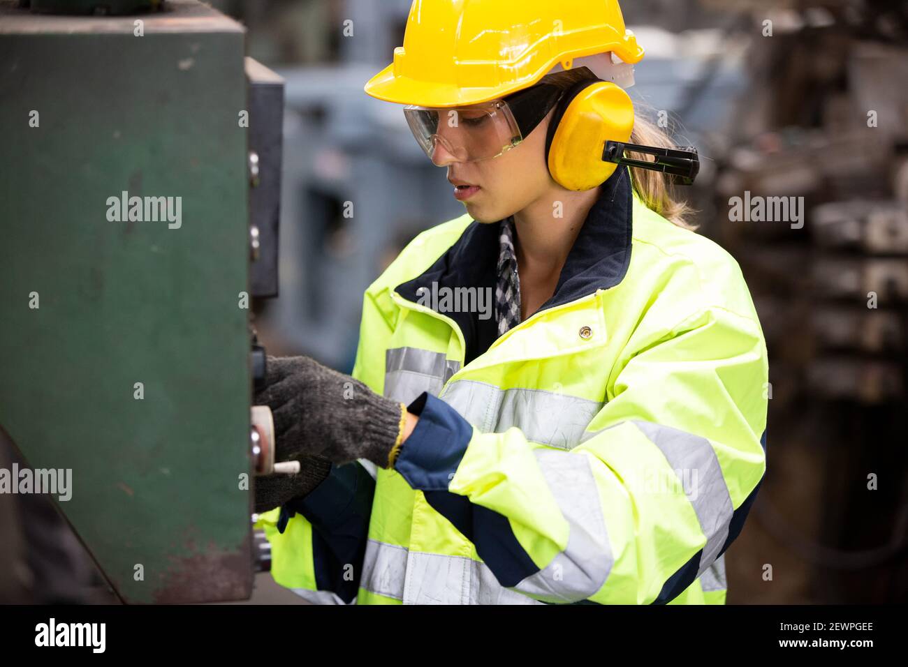 Woman worker wearing safety goggles control lathe machine to drill ...
