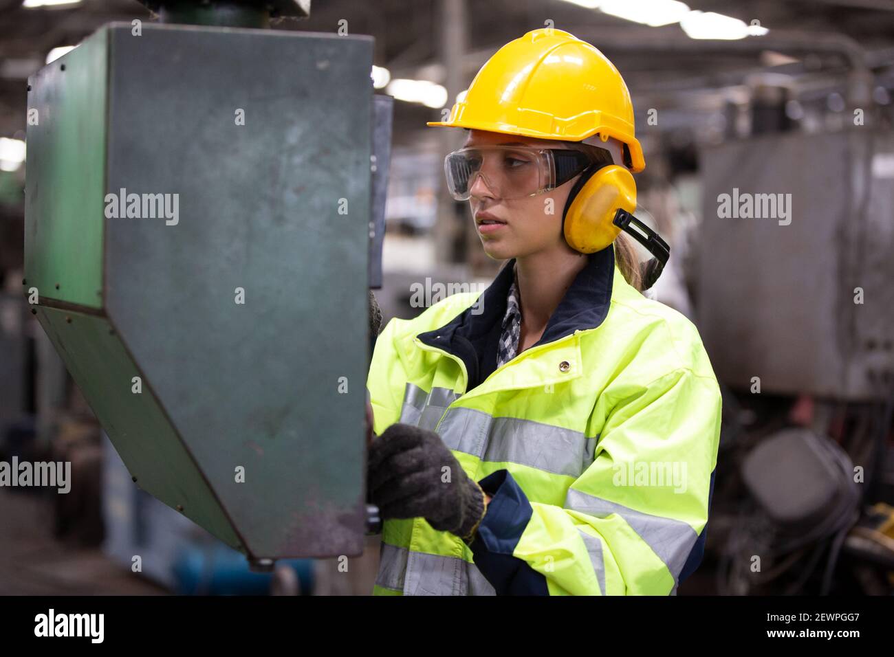 Woman worker wearing safety goggles control lathe machine to drill ...