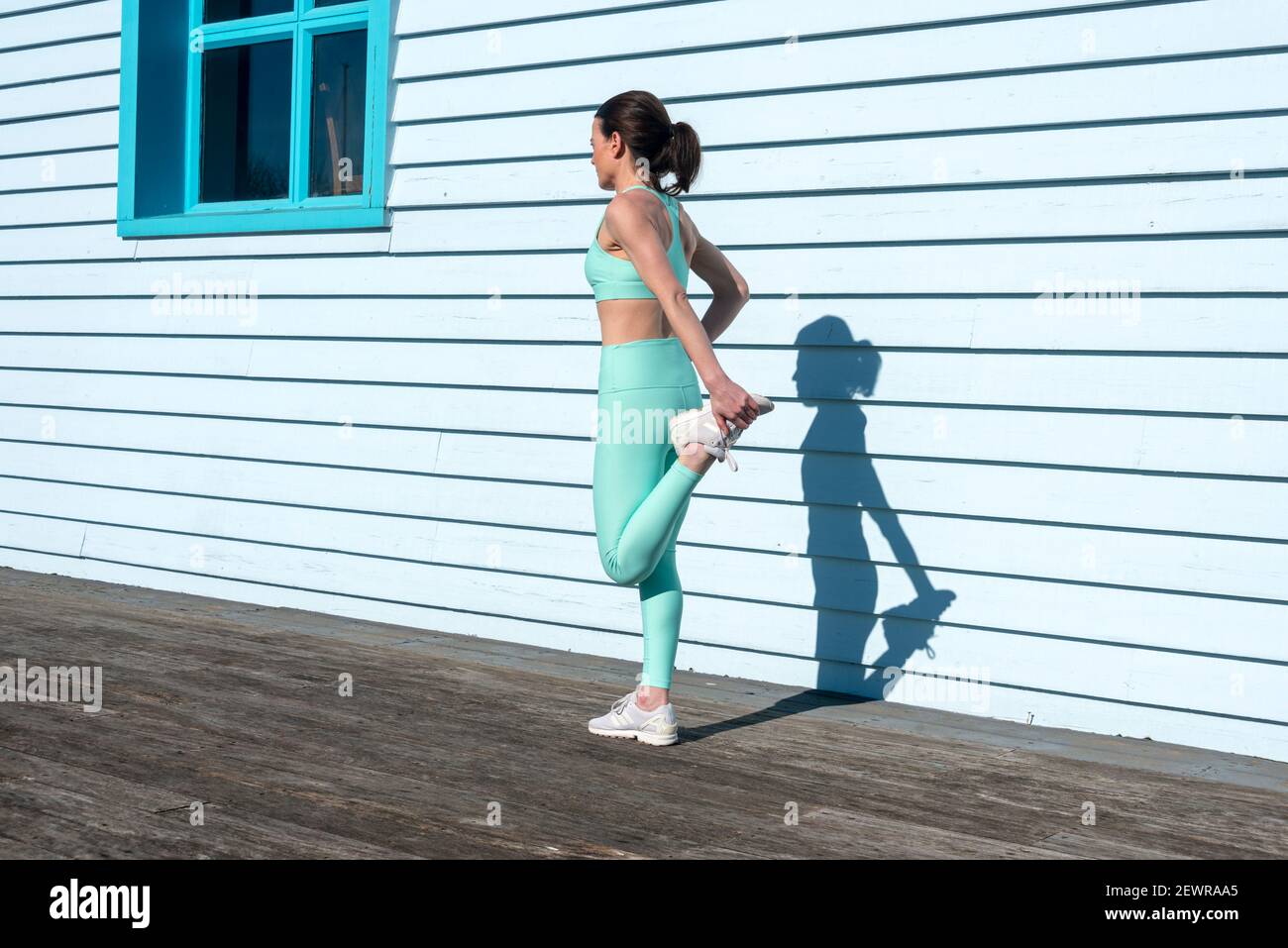 Side view of a sporty woman doing a leg stretch, warming up exercise ...