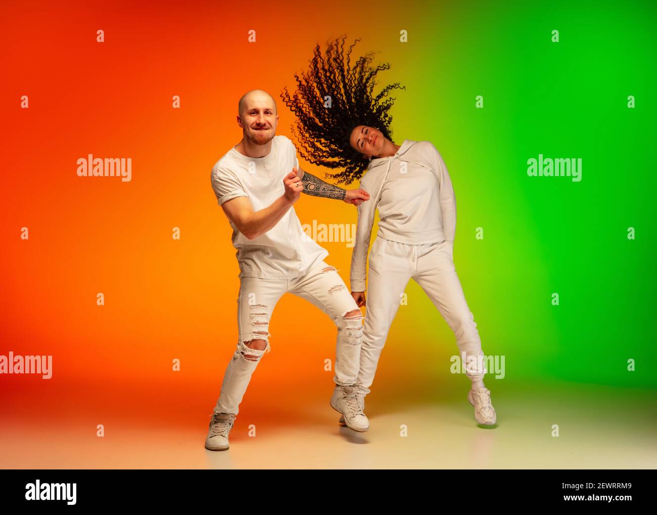 Stylish sportive caucasian couple dancing hip-hop on colorful gradient ...