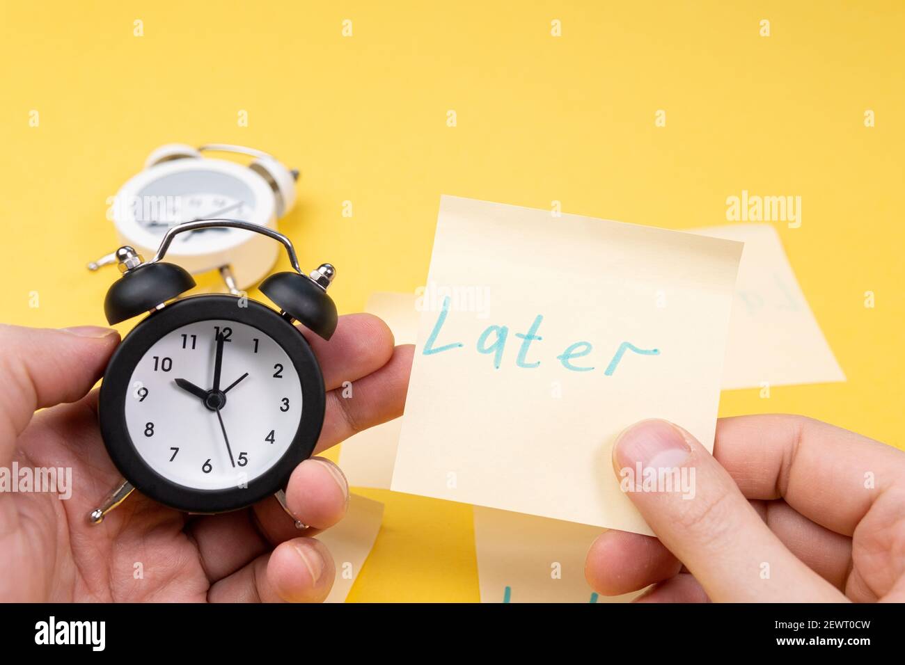 Alarm clock with a sticky note with text later. Procrastination, delay ...
