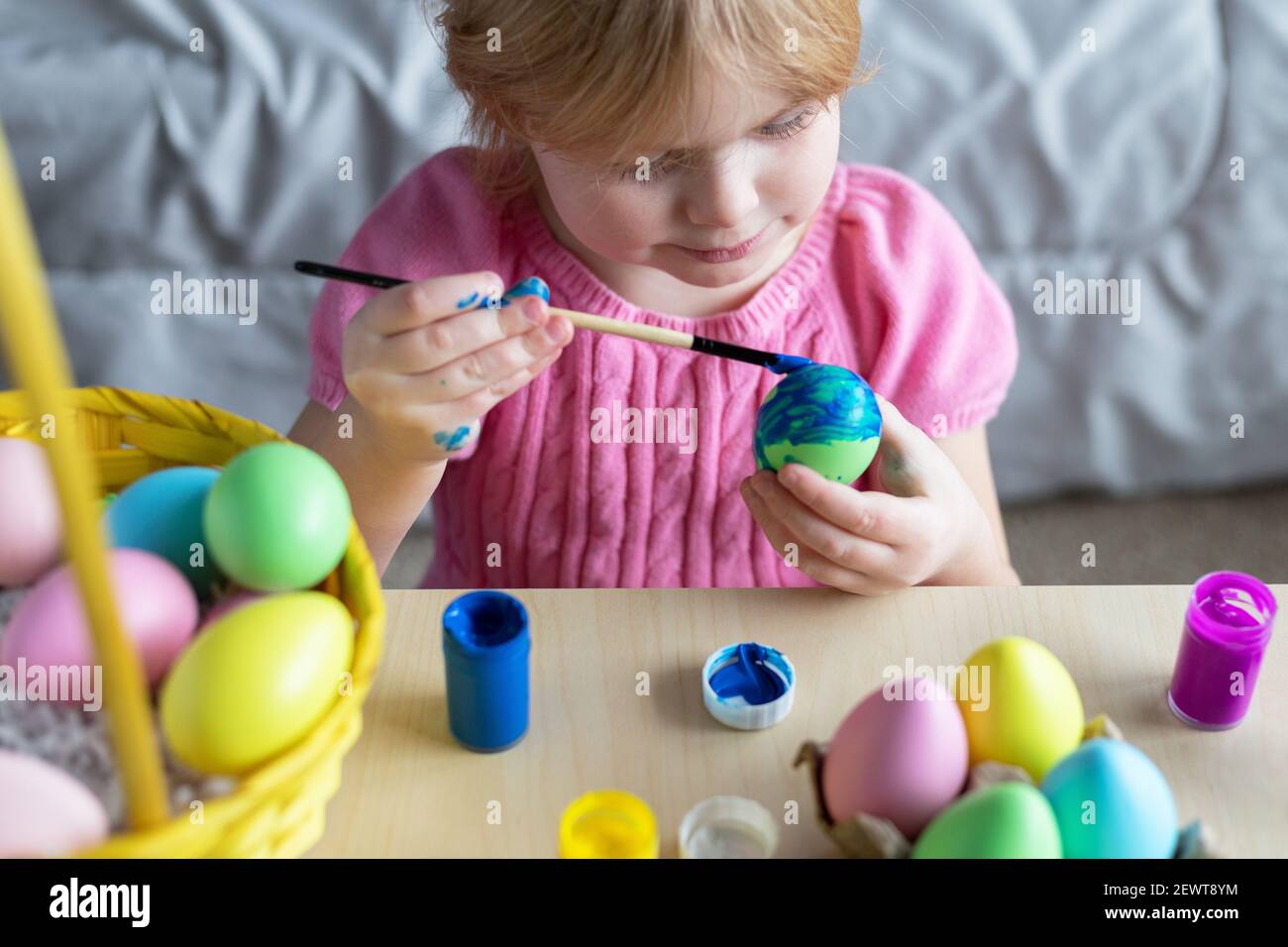 Little girl in Easter bunny ears painting colored eggs. Easter family ...