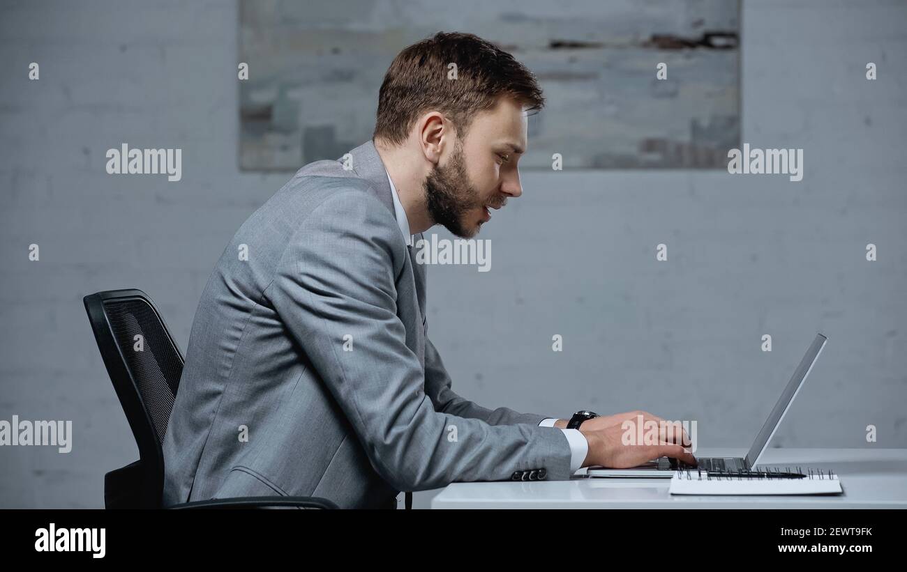 side view of bearded businessman typing on laptop keyboard in office ...