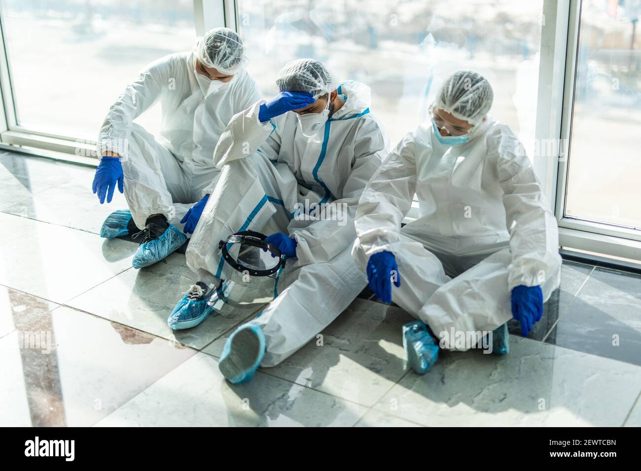 Tired three doctors sit back to back on the floor during a heavy shift ...