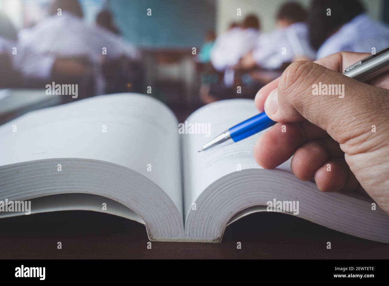 Hand holding a pen and reading book with uniform school students doing ...