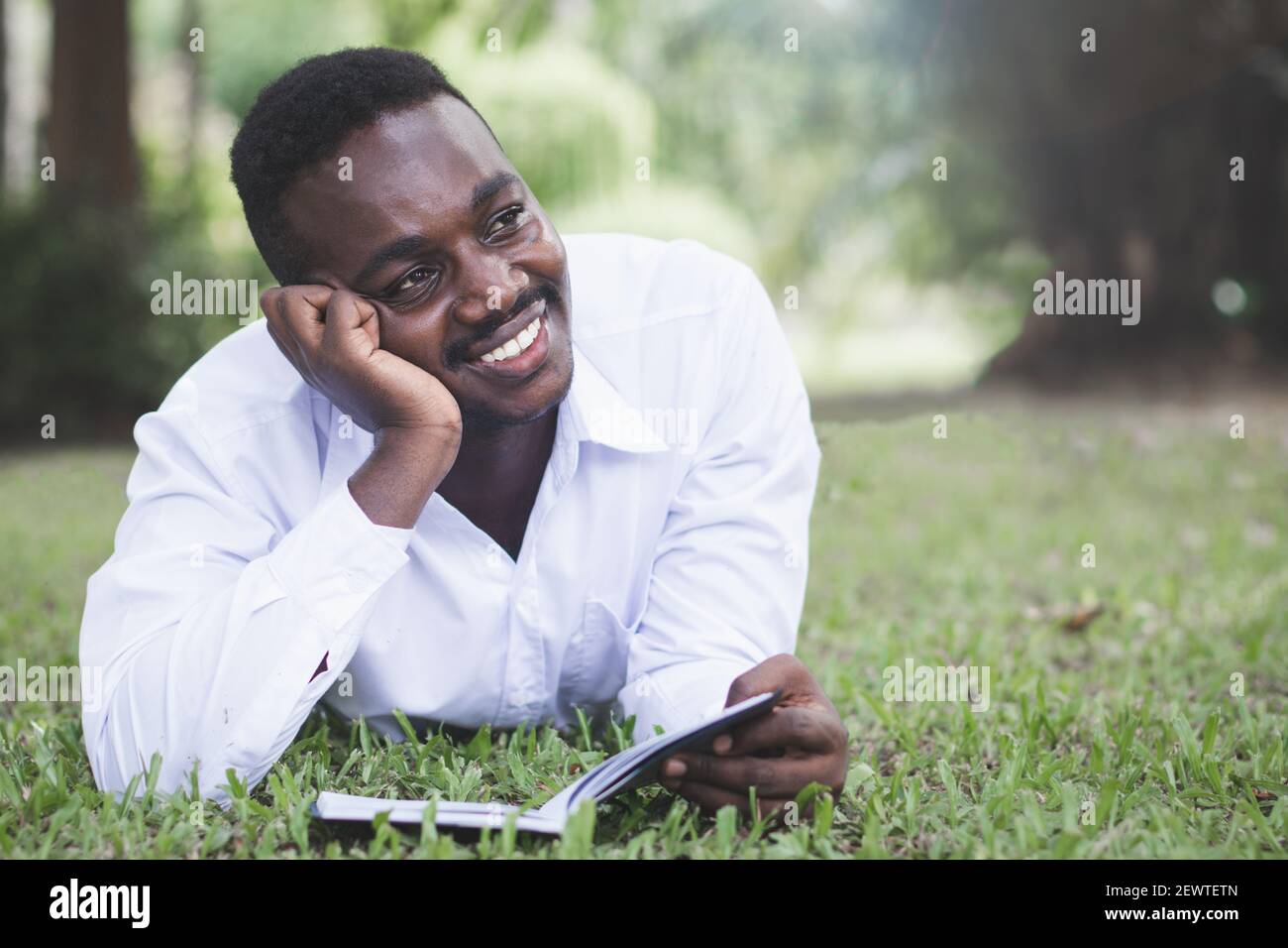 African man thinking and reading a book in the park.World book day ...