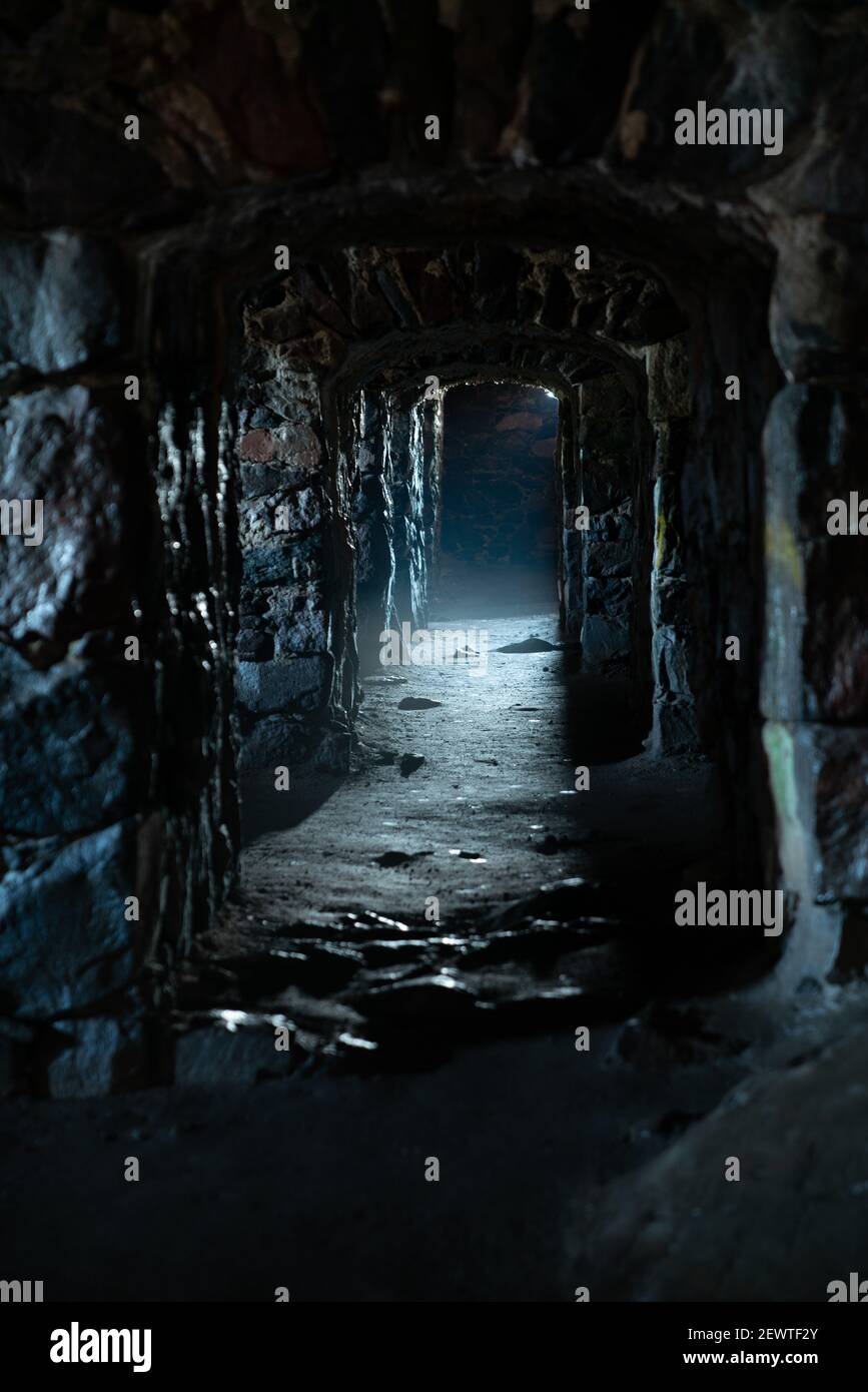 A dark, damp, cold dungeon corridor with stone walls all along the ...