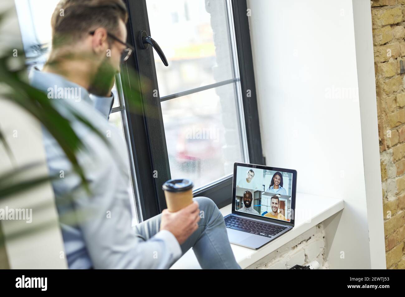 Young office worker sitting on a window sill in front of a laptop ...