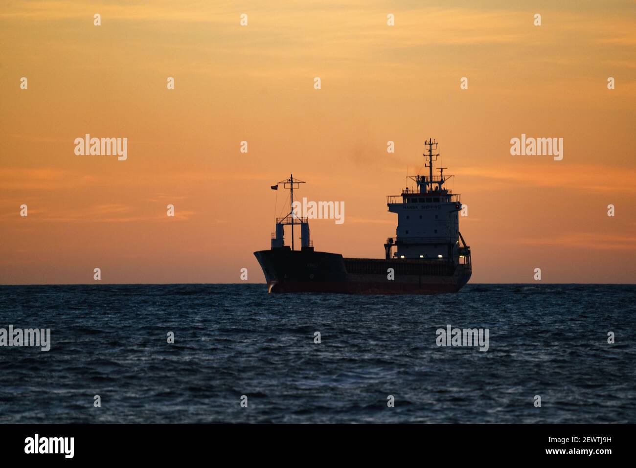 Cargo ship sailing away against colorful sunset Stock Photo - Alamy