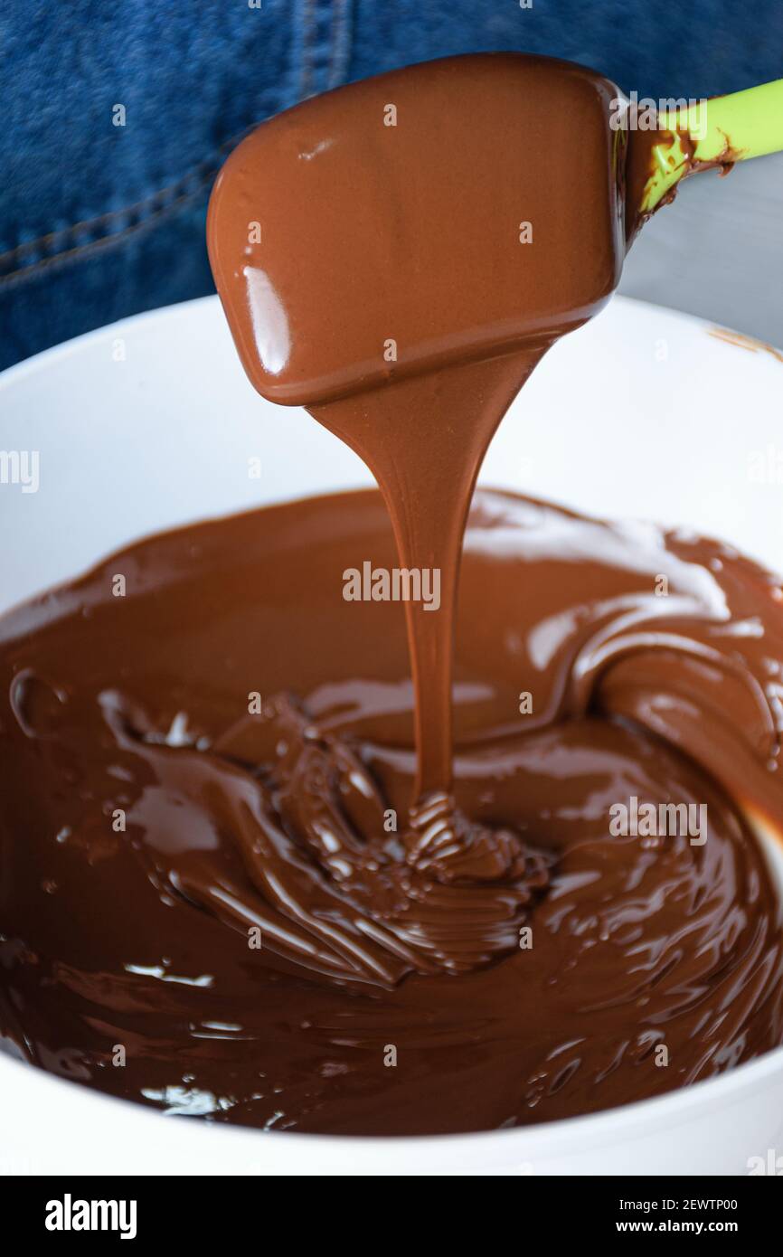 Closeup of a spatula with tempered chocolate falling into a white bowl ...