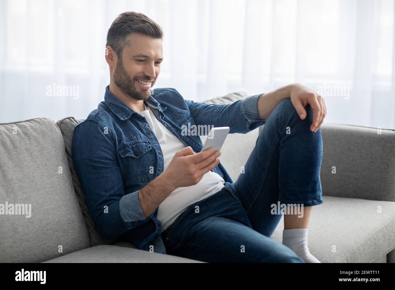 Happy man sitting on couch at home, using mobile phone Stock Photo - Alamy