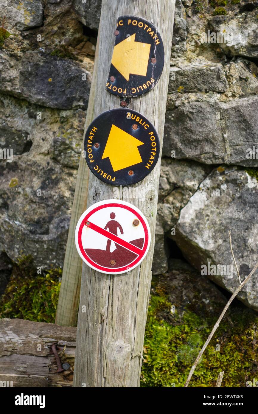 A conflicting wooden waymarker with a yellow arrow saying public ...