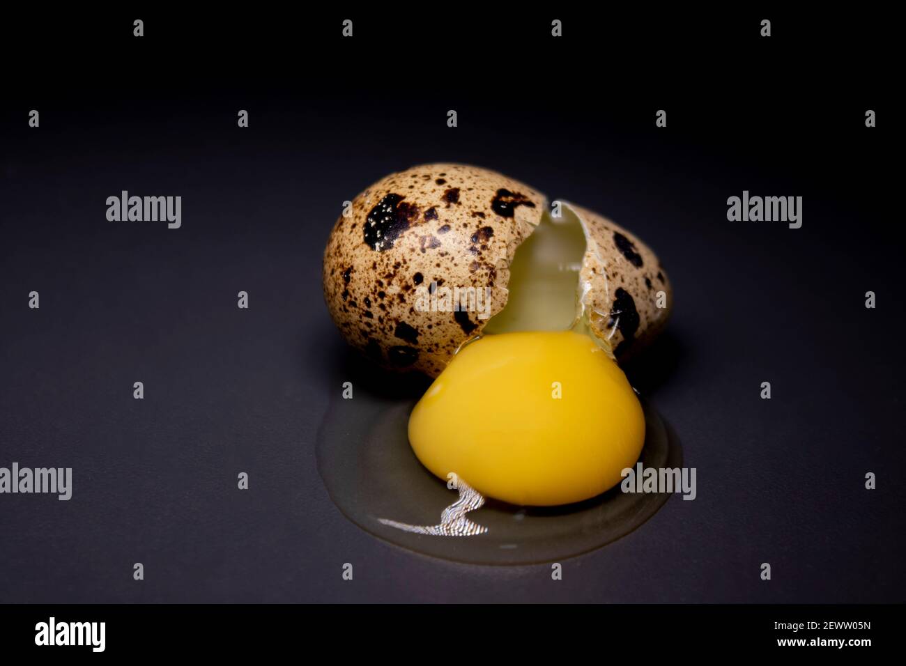 broken Quail egg isolated on black background with leaking white and ...