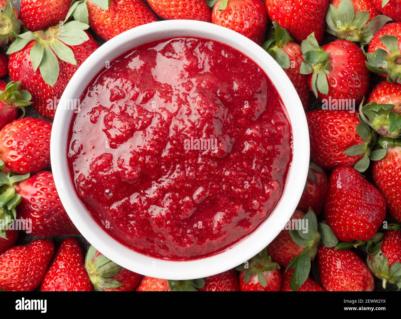 Top view of a bowl full of strawberry jam over strawberries background ...