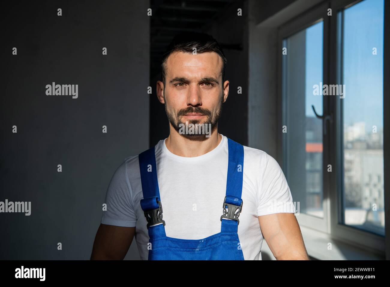 A builder in a blue overalls stands in the shade Stock Photo - Alamy
