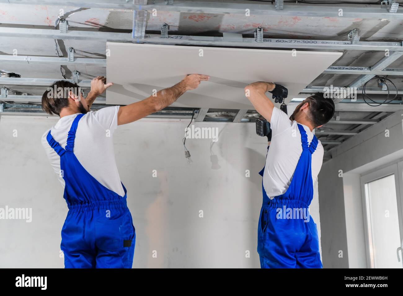 Adjusters in blue overalls making ceiling in apartment room Stock Photo ...