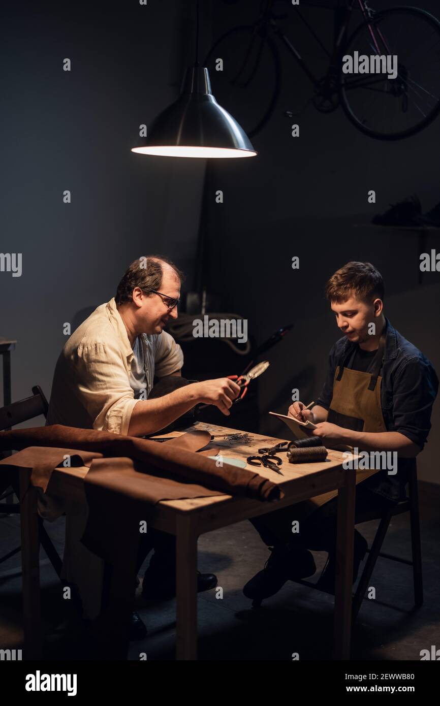 an experienced shoemaker and his assistant in their workshop make shoes ...