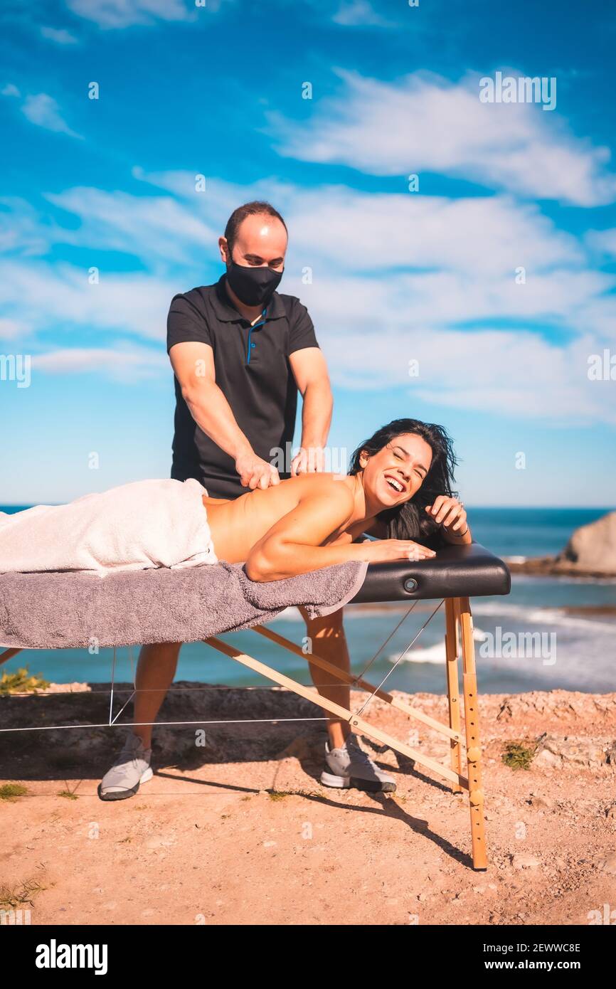 A vertical shot of a masseur in a facial mask doing massage to a ...