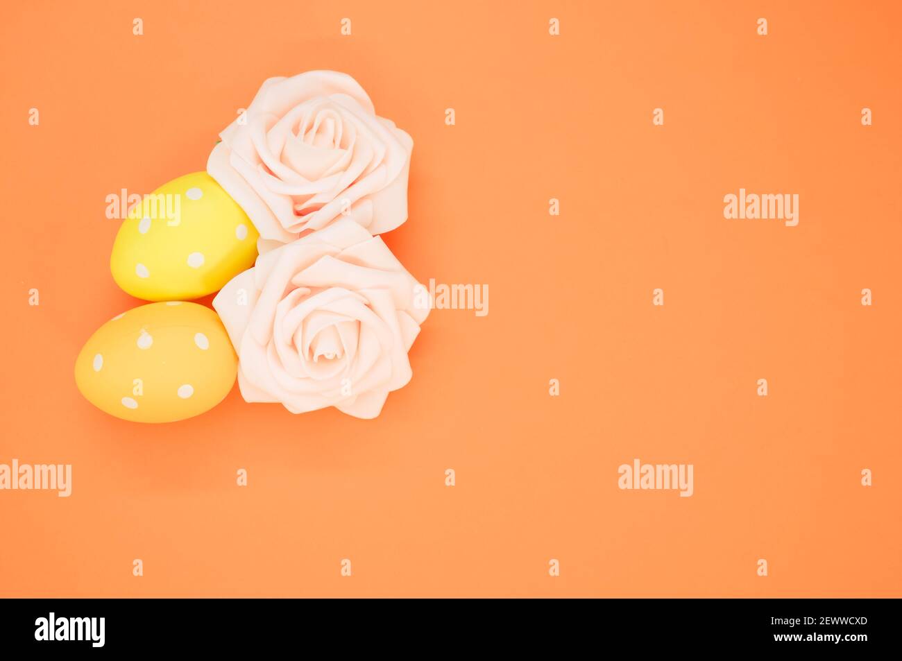 A closeup shot of decorated Easter eggs and pink roses on an orange ...