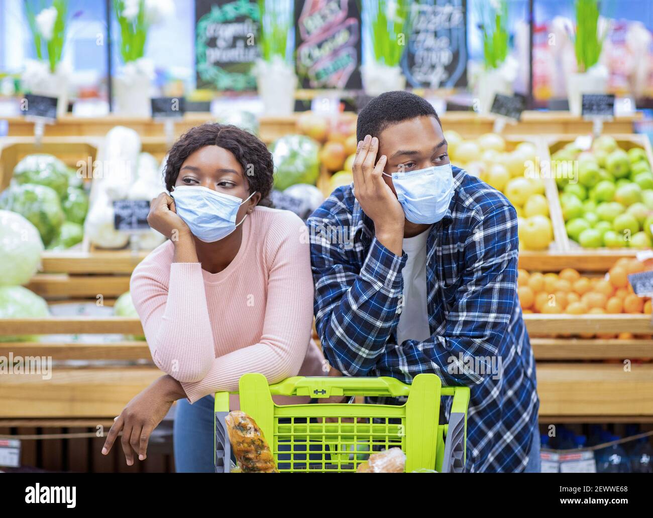 Bored millennial couple in face masks leaning on shopping cart, sick ...
