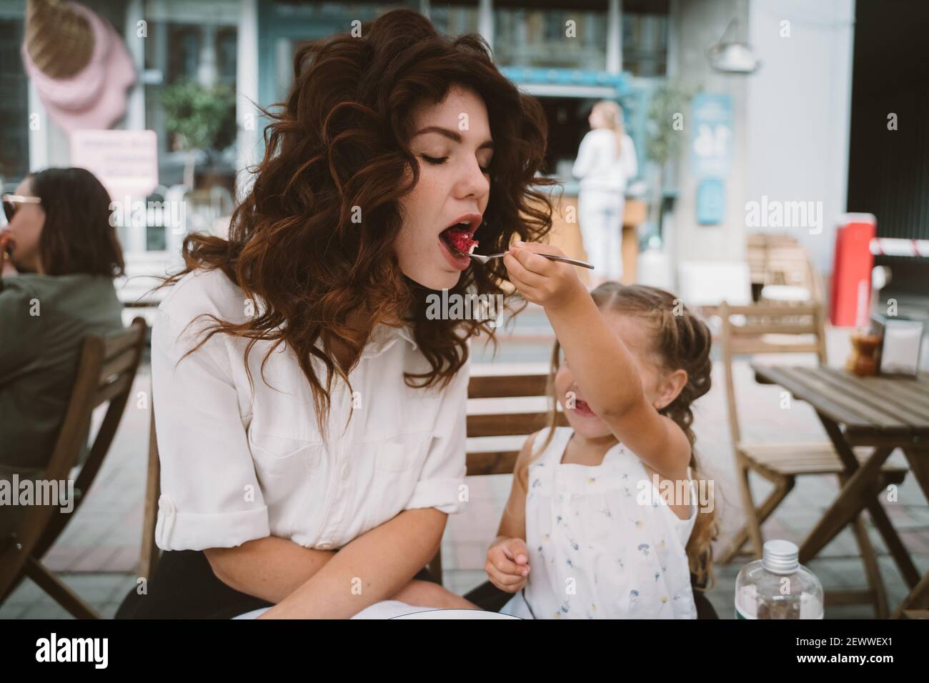 Young mom eating cake with smiling kid on the street Stock Photo - Alamy