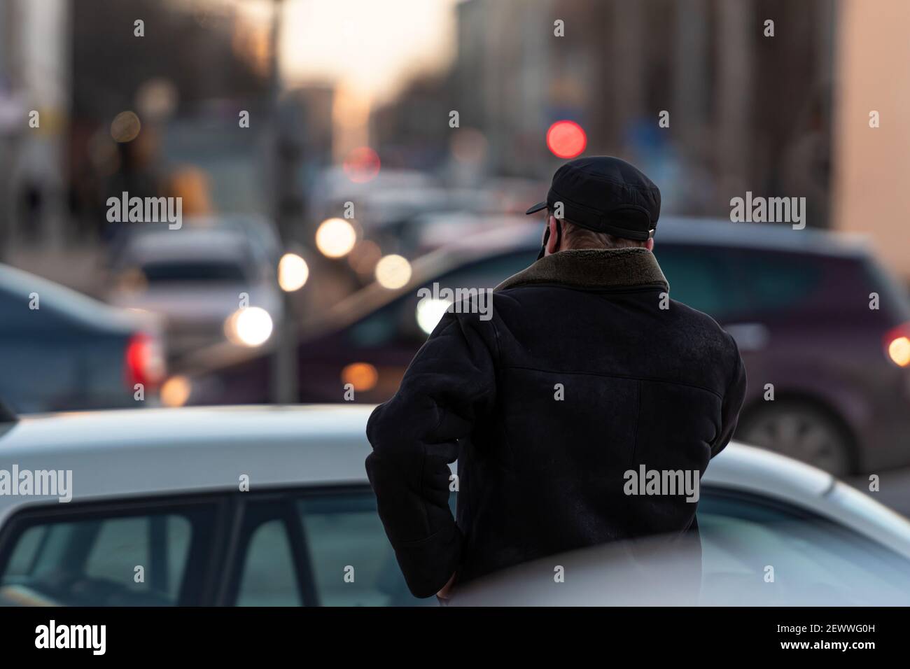 a lonely man from behind on a busy street with evening city traffic ...