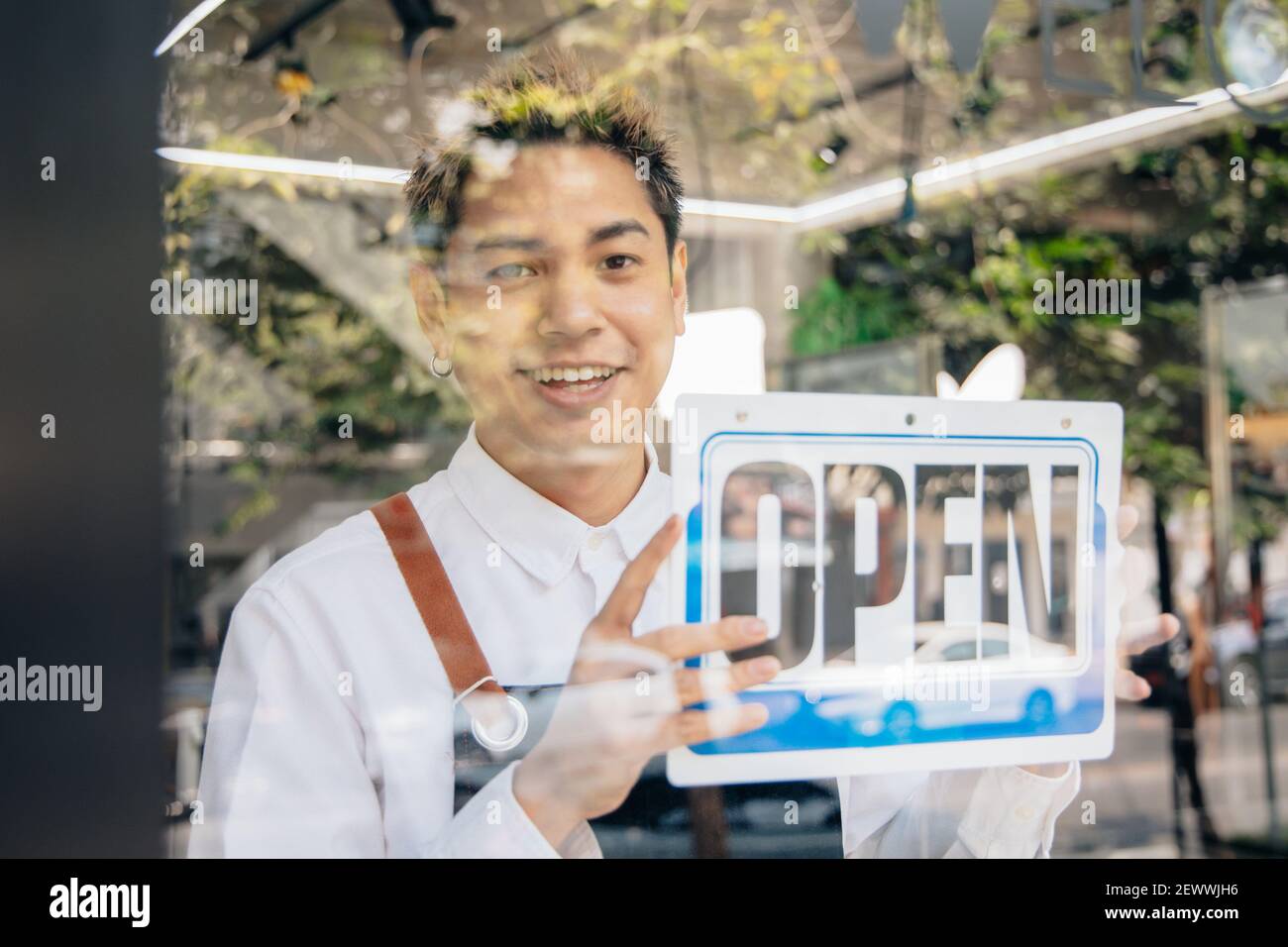 Young Asian man hanging open sign by glass window. Male shop owner ...