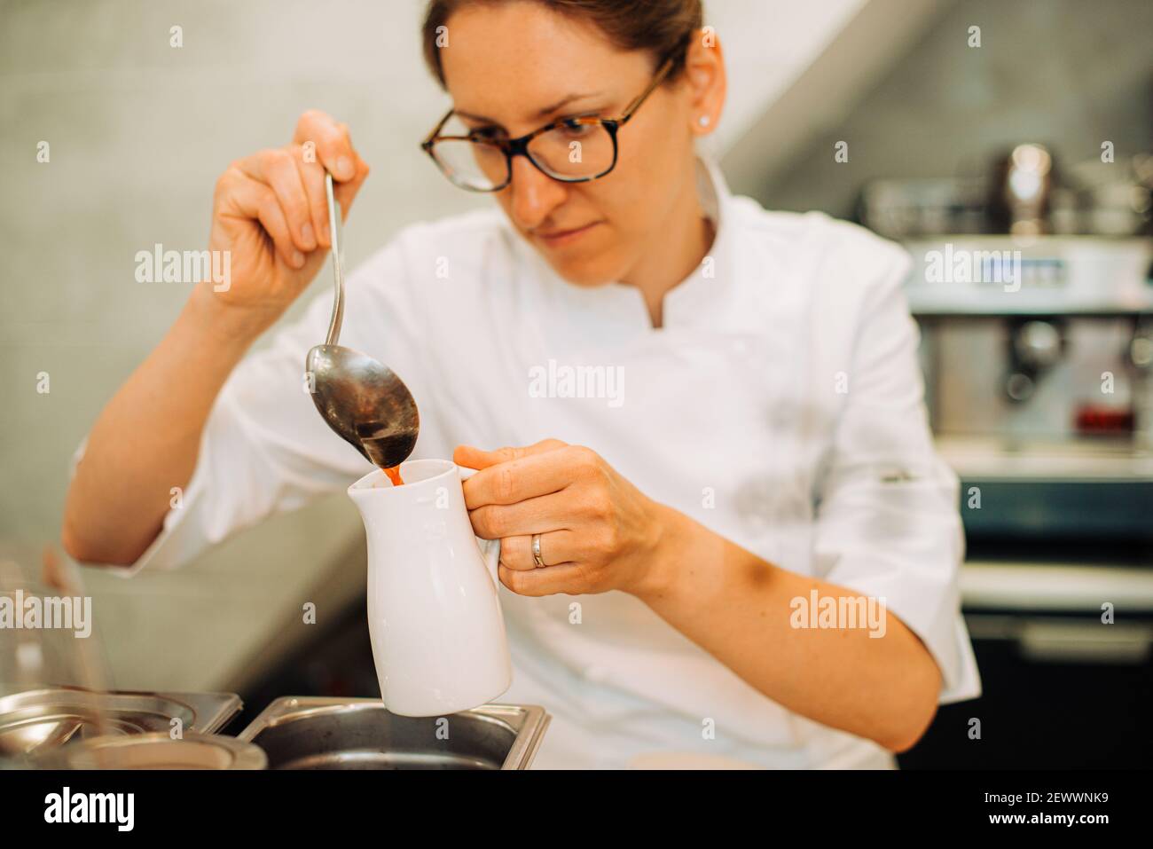 French female chef pouring sauce while working at kitchen Stock Photo ...