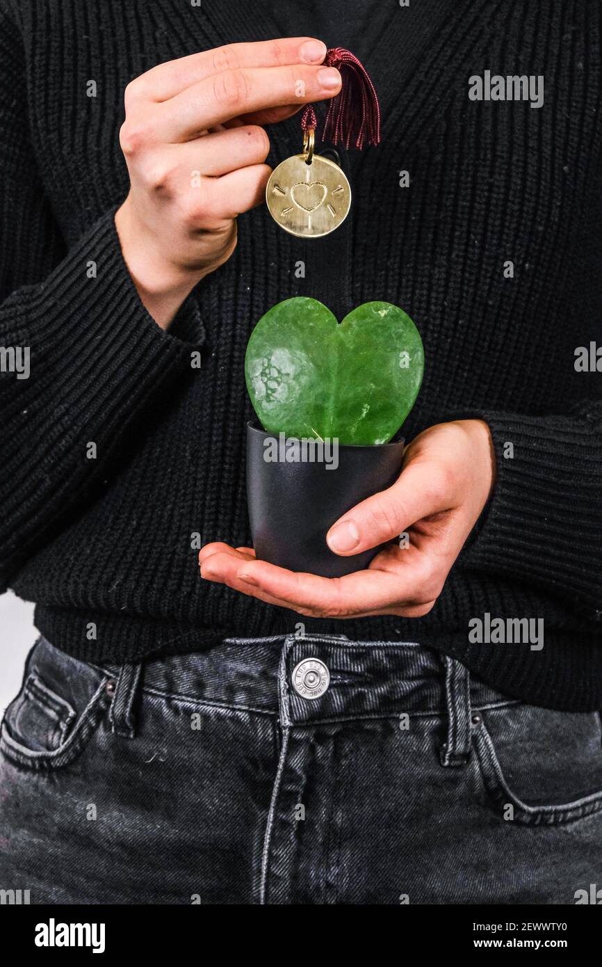 A vertical shot of a person holding a small gold pendant and a potted ...