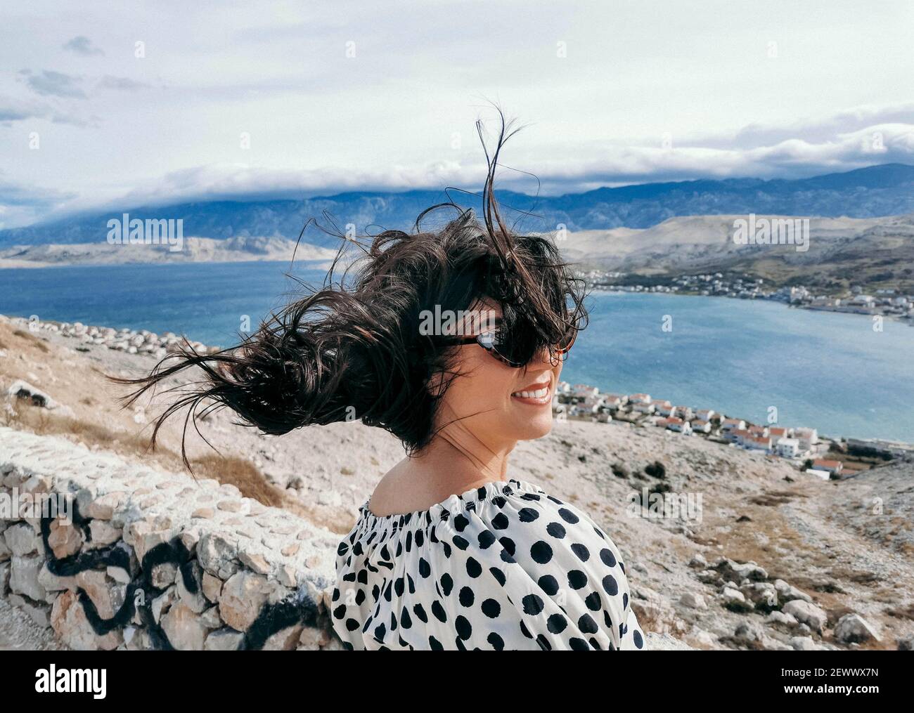 A cheerful Caucasian woman in a polka-dotted flowy dress and sunglasses ...
