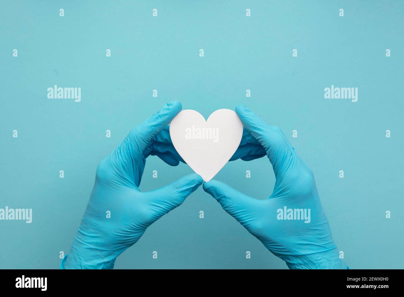 Doctors hands wearing blue surgical gloves holding a white heart shape ...