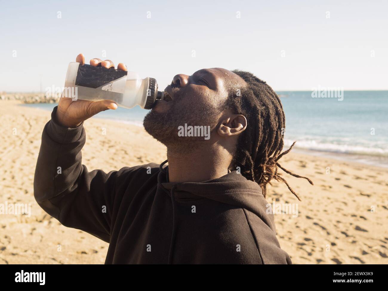 A young African-American male drinking water on a beach Stock Photo - Alamy