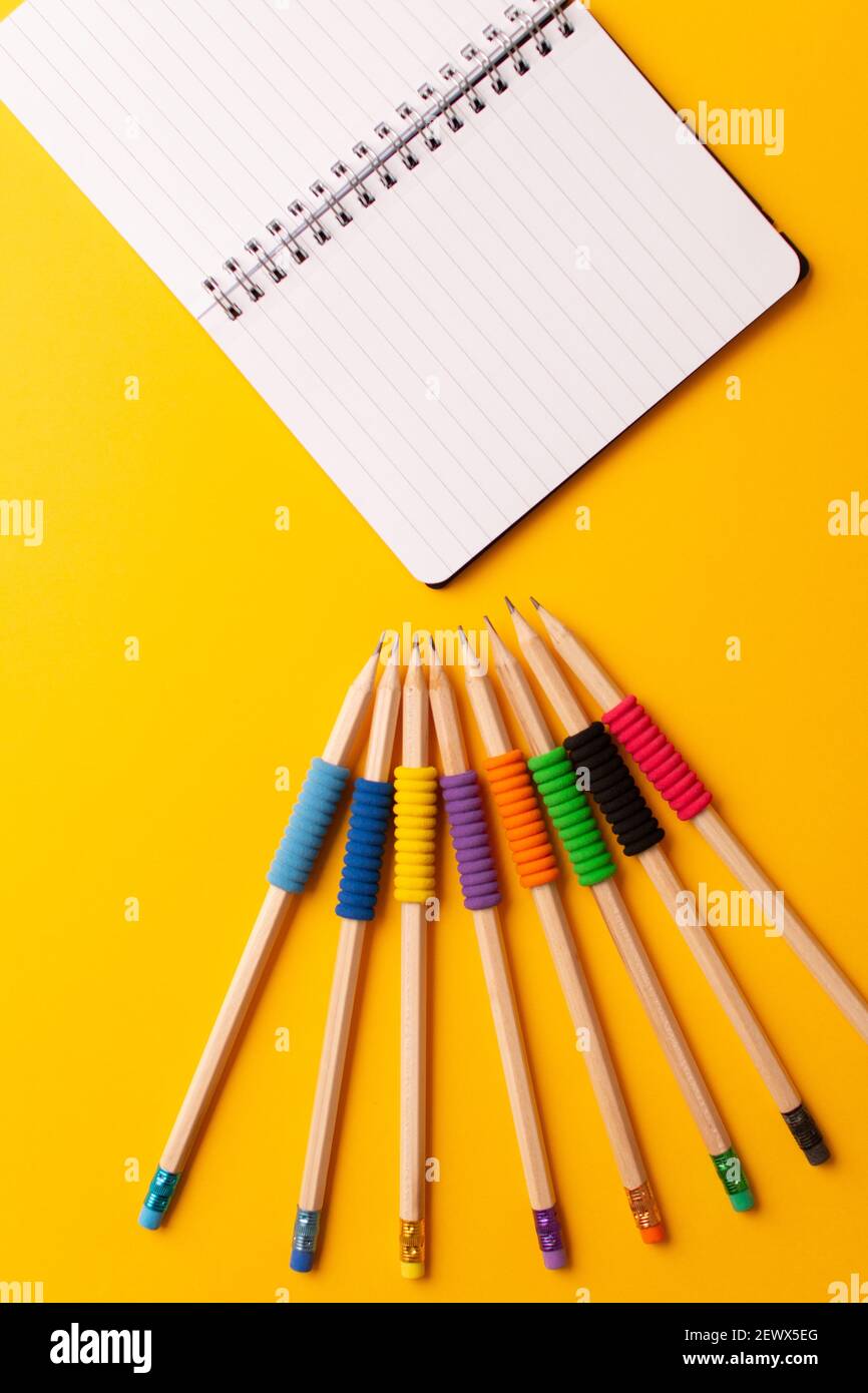 A vertical shot of an open journal and pencils with colorful rubbers ...