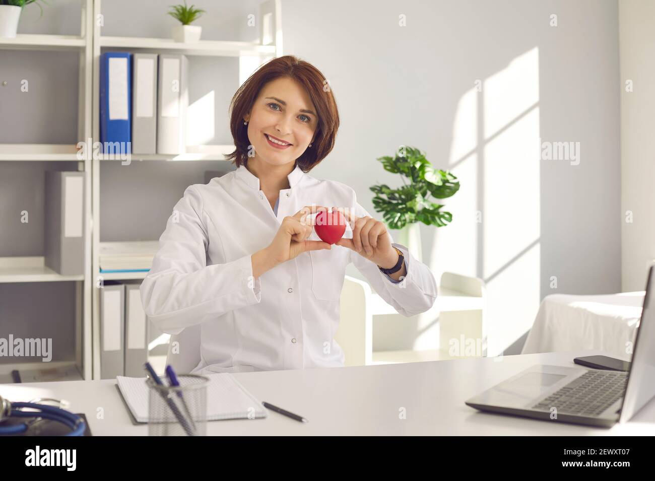 Happy doctor sitting at desk, holding red heart and reminding of ...
