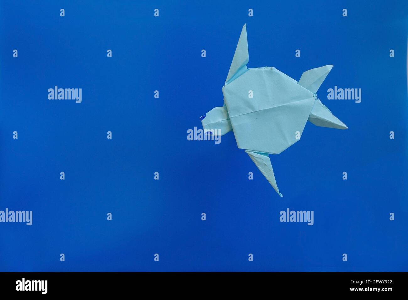 Origami paper turtle from above against blue background with copy space ...